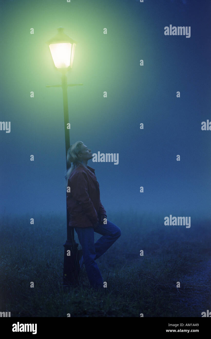 Woman leaning against lamp post on misty night Stock Photo - Alamy