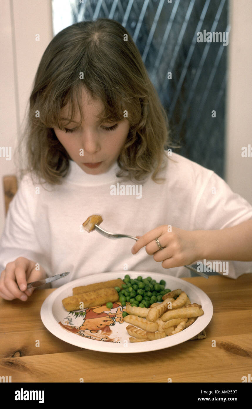 seven year old girl eating fish fingers chips and peas at the table ...