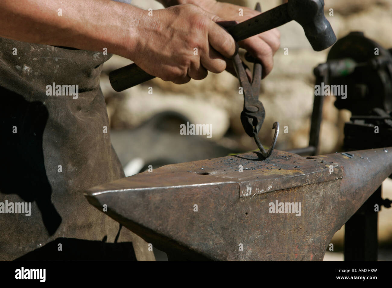 A Blacksmith shapes a heated iron with a hammer on the anvil during a ...
