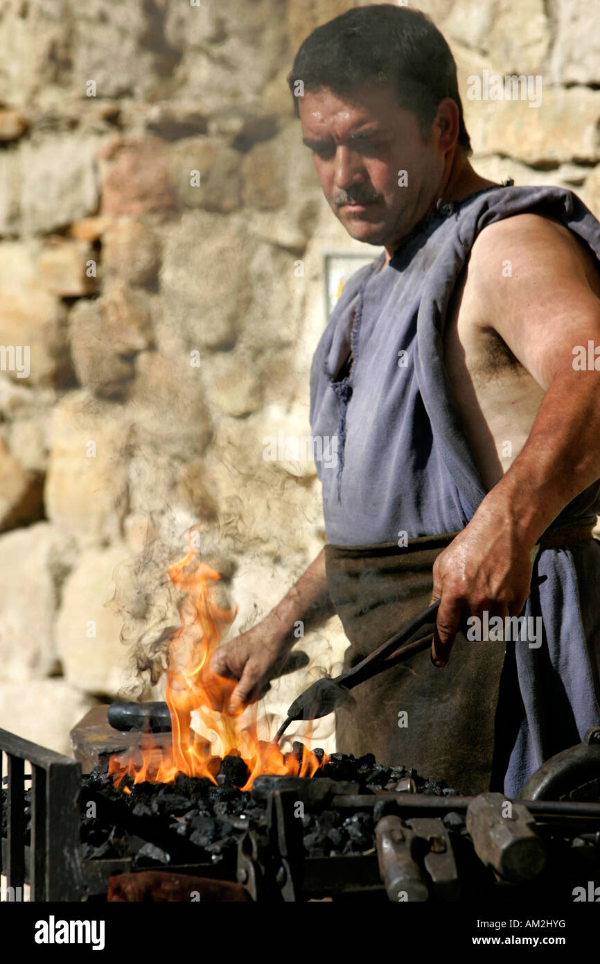 A Blacksmith holds a heated iron in a fire before shaping it with a ...