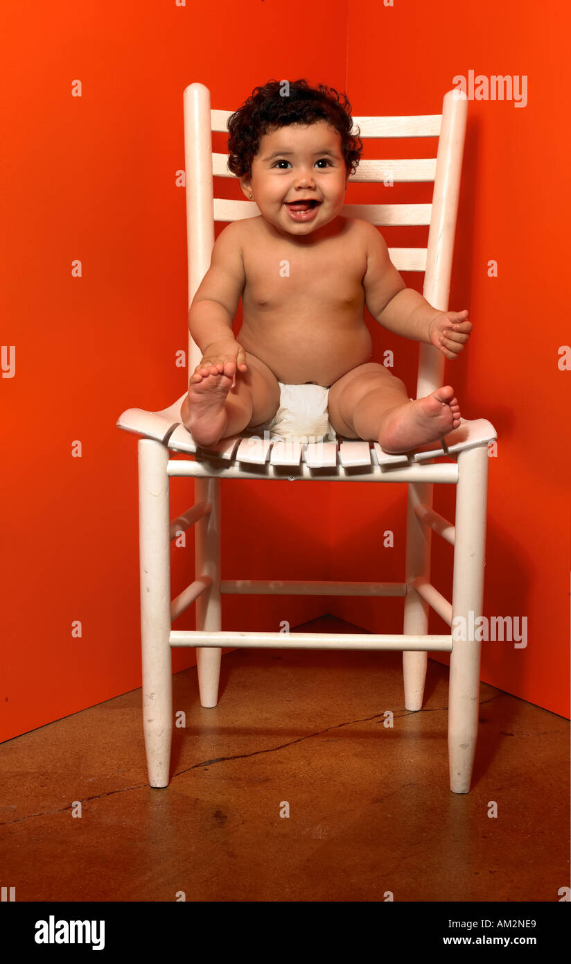 A cute baby laughs while sitting on a chair by herself against the ...