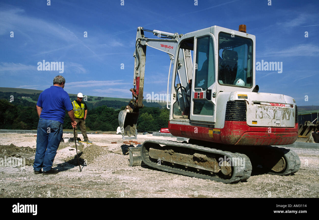 Builders with mechanical digger excavating foundations for new housing ...
