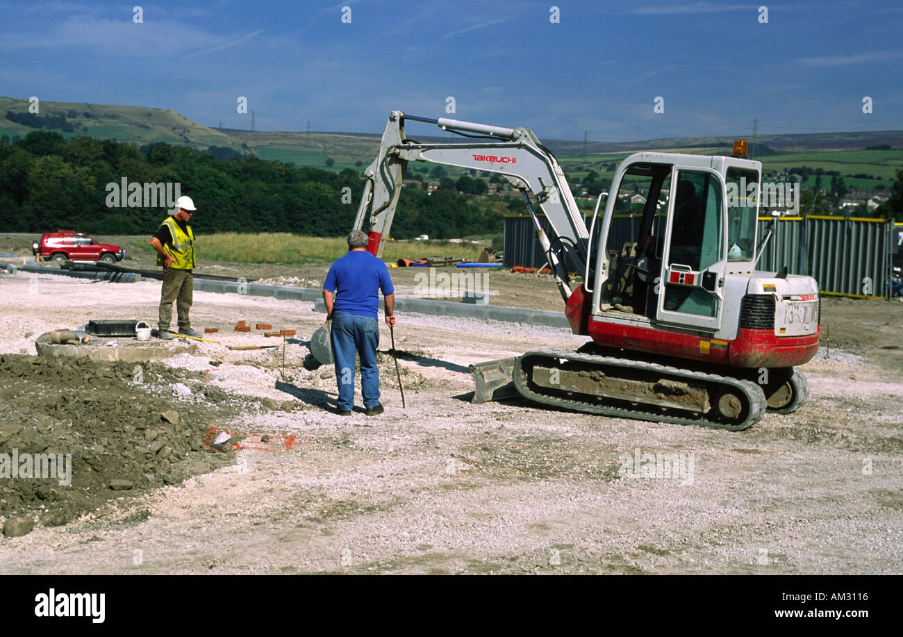 Builders with mechanical digger excavating foundations for new housing ...