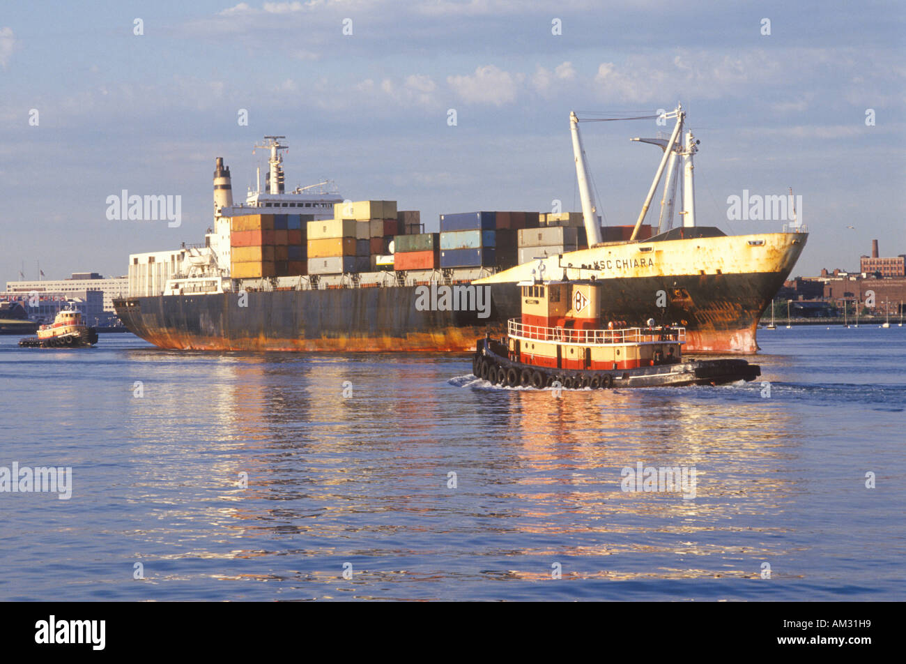 A pair of tug boats working together to turn around a ship loaded with ...