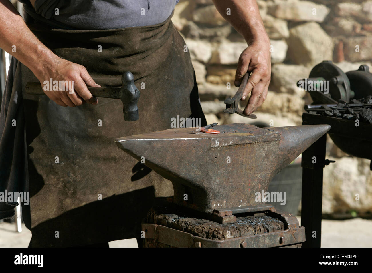 A Blacksmith shapes a heated iron with a hammer on the anvil during a ...