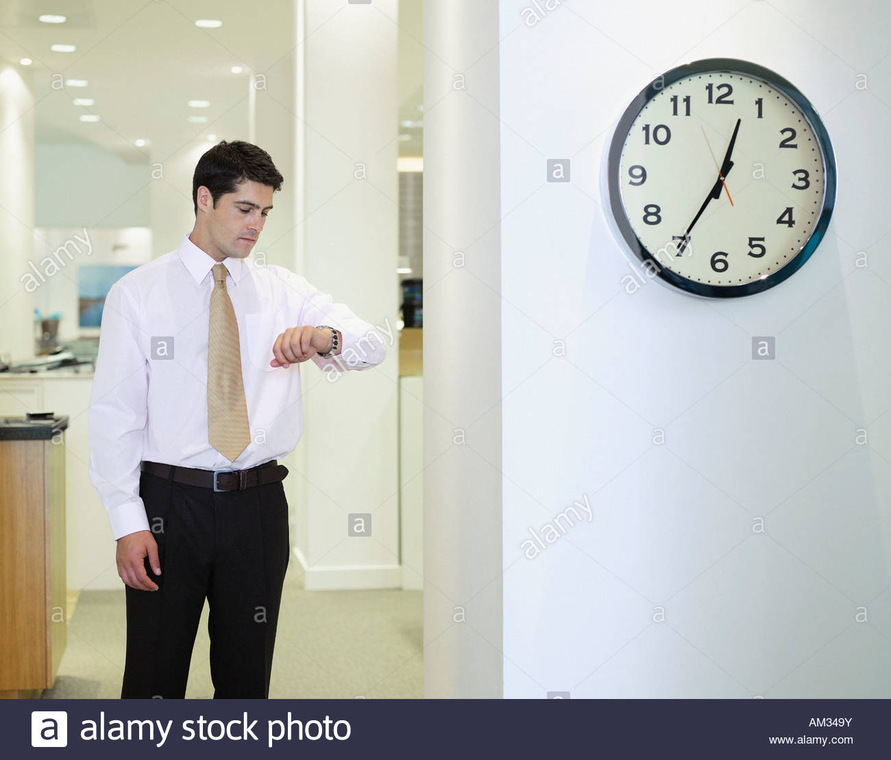 Businessman checking watch in office by clock Stock Photo, Royalty Free ...
