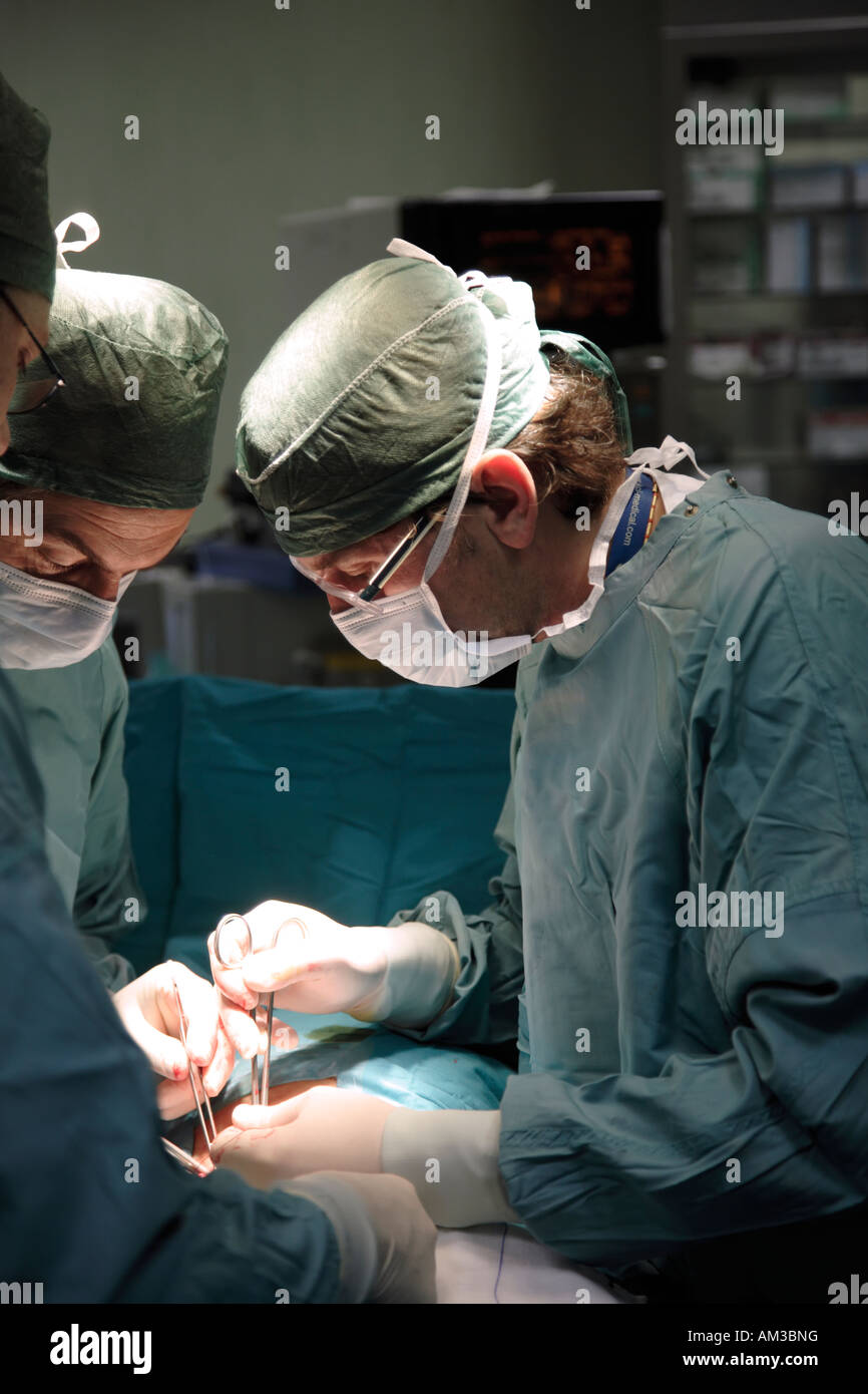 three doctors in operating theatre operating on patient Stock Photo - Alamy
