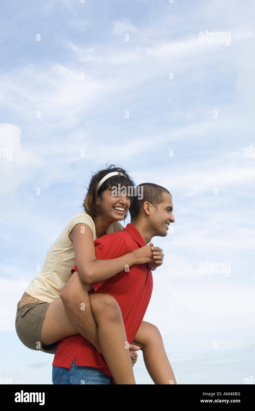 Portrait of a young woman riding piggyback on a young man and smiling ...