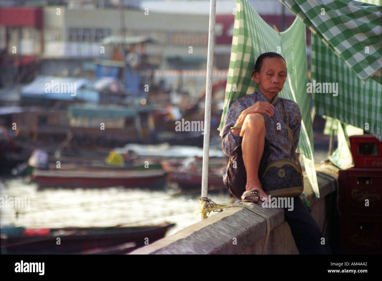 An old woman sits on a ledge by the ferry terminal in Cheung Chau ...