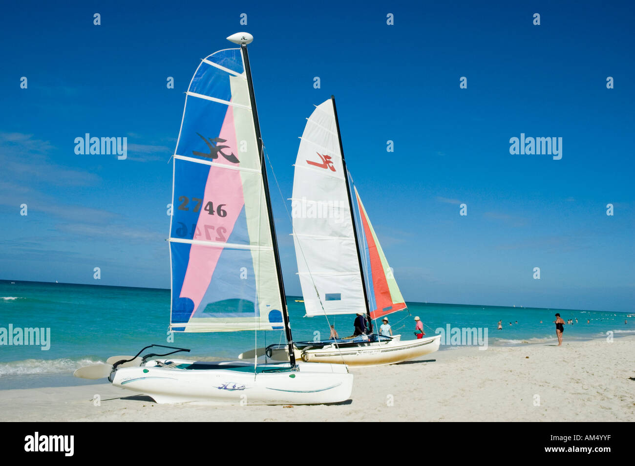 Small sailing dinghies with colourful sails sit on the white sand ...