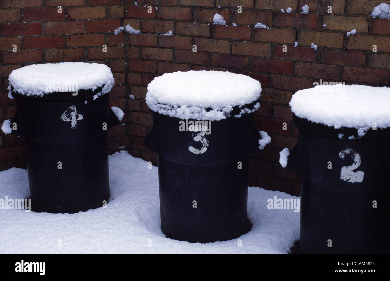 Three snow covered, numbered dustbins left outside a block of flats ...