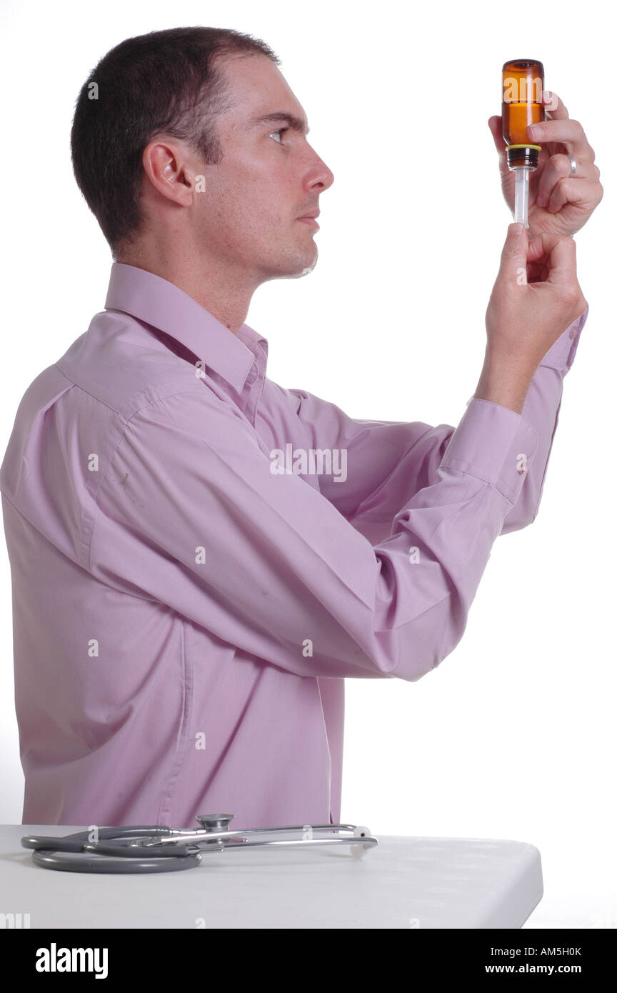 A young male doctor at his desk measuring a dose of medication into a ...