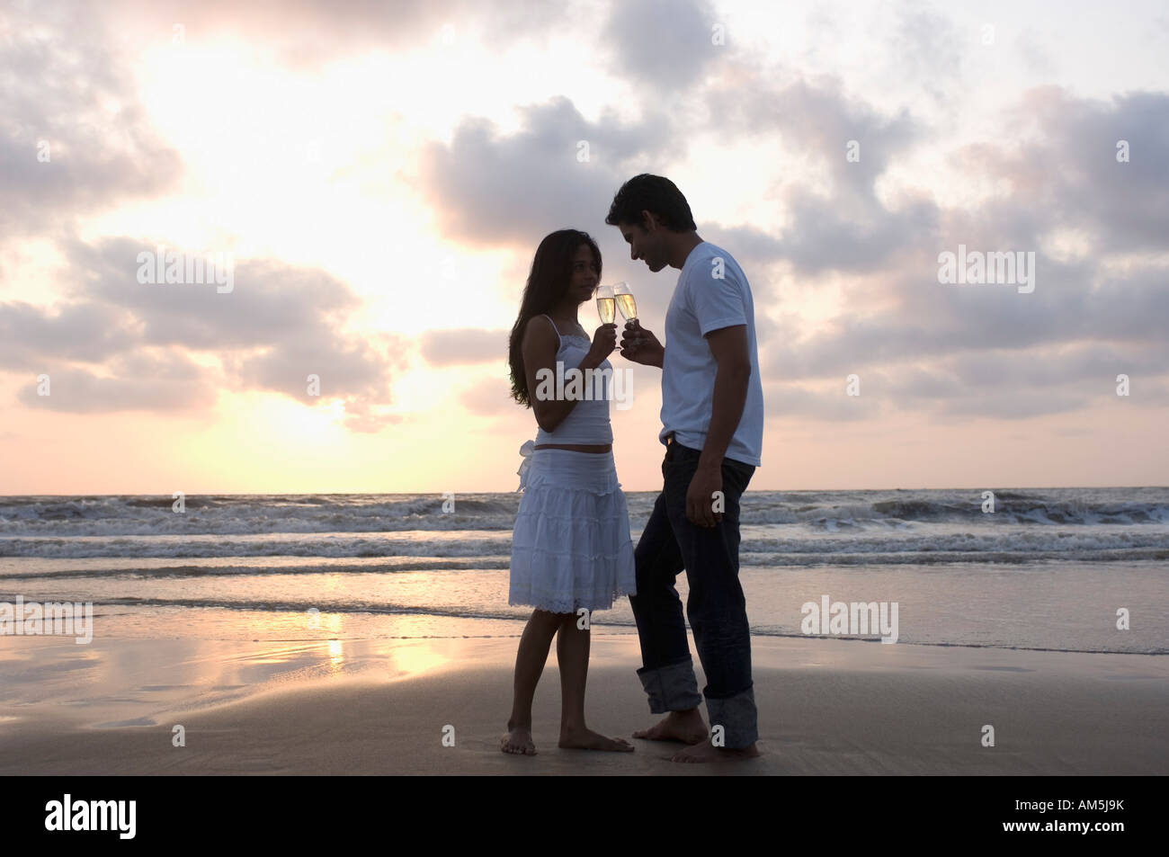Side profile of a young couple standing on the beach and toasting with ...