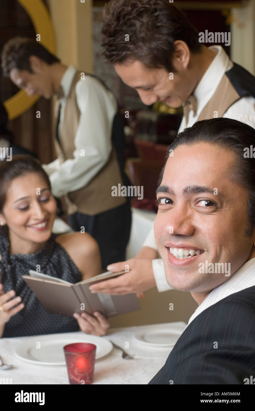Portrait of a mid adult man smiling and a waiter taking order from a ...