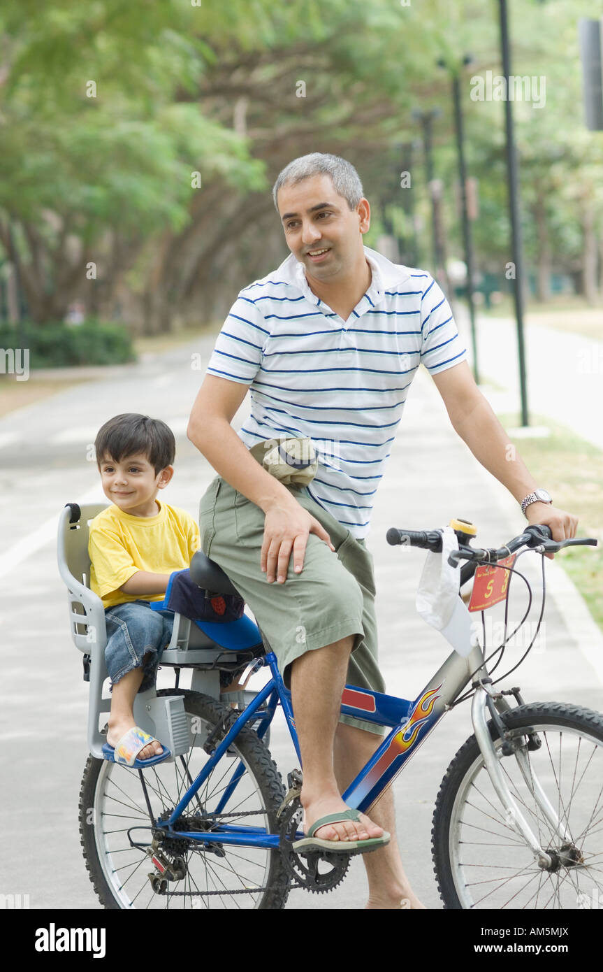 Mid adult man riding a bicycle with his son sitting behind him Stock ...