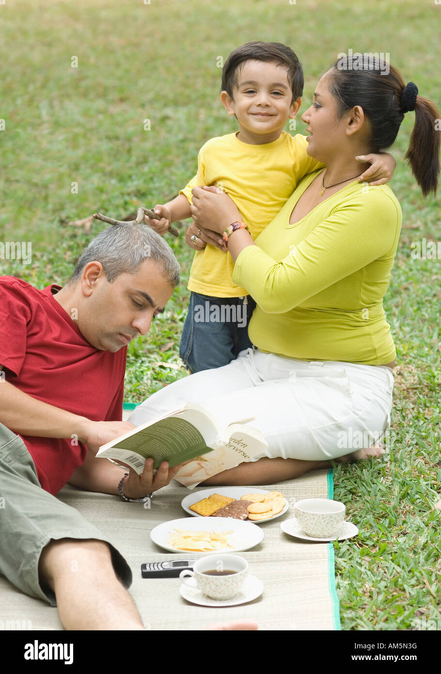 Mid adult man reading a book and a mid adult woman hugging her son ...