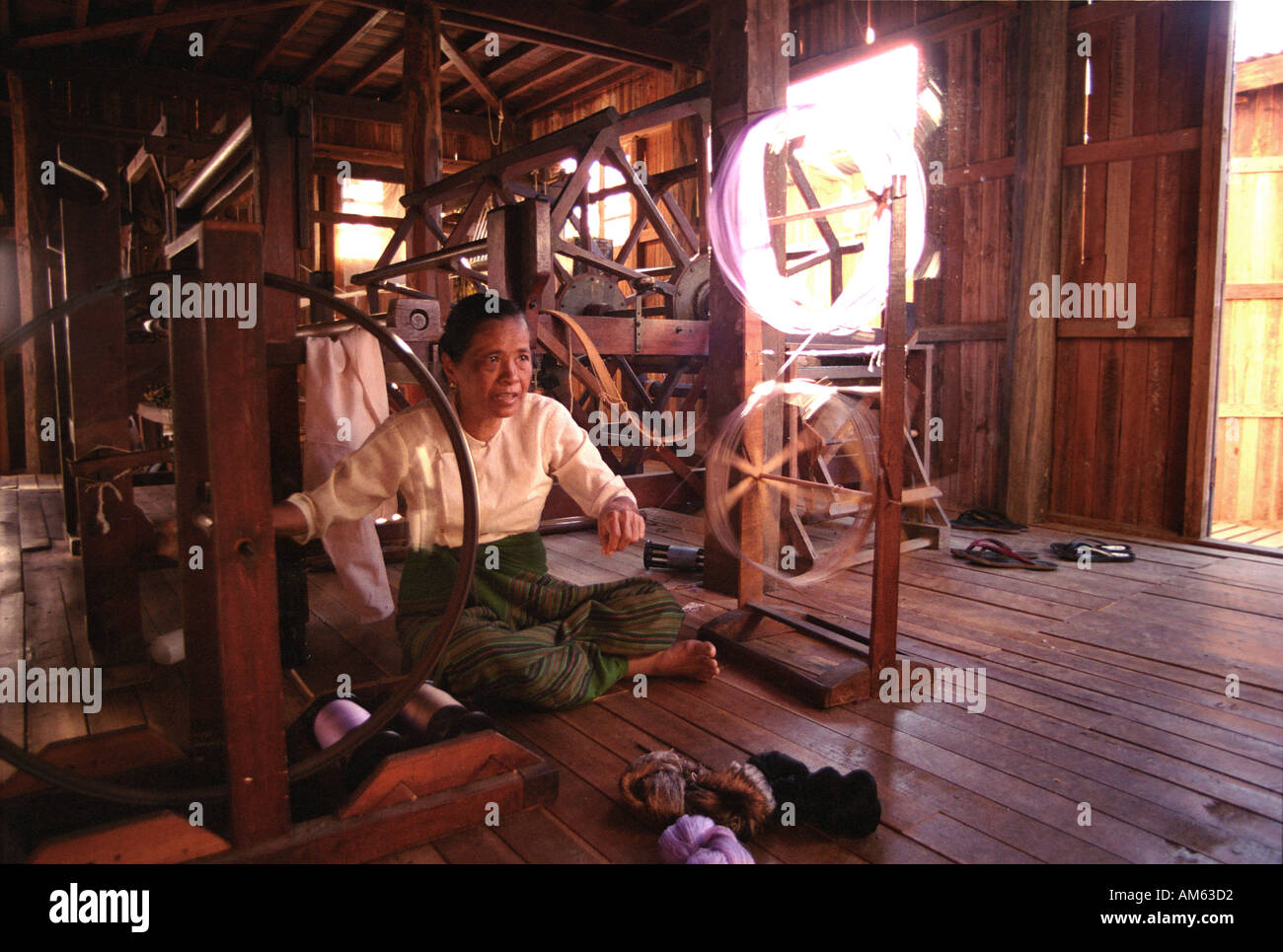 Burma An old woman works silk on a spinning wheel in an old teak ...