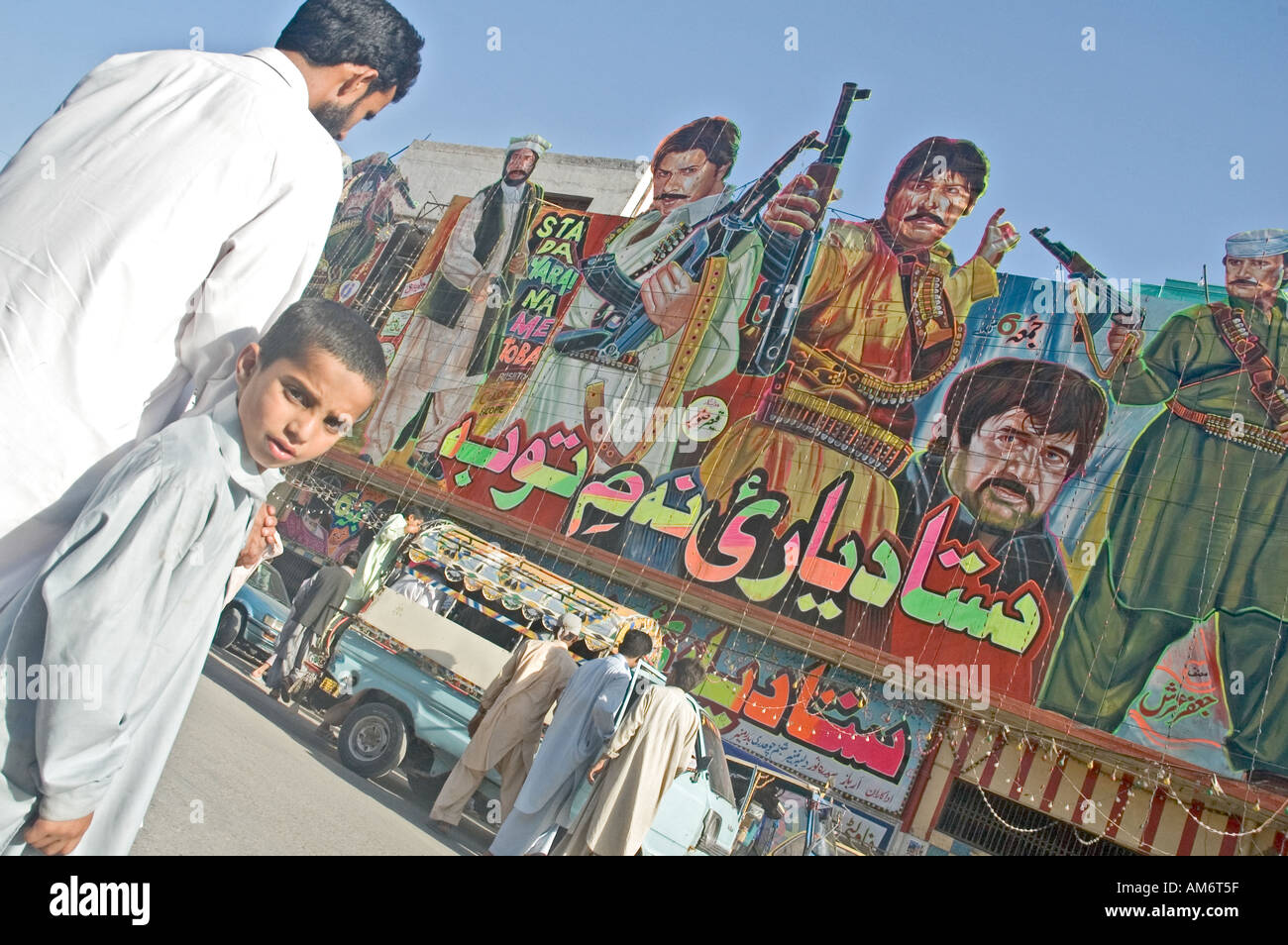 A pashto man and his child in front of a large cinema billboard ...