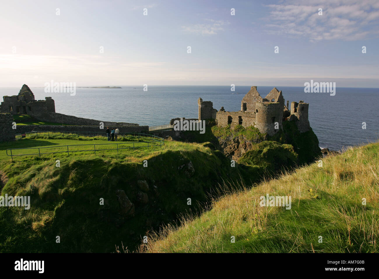 Tourists admire the ancient ruins of Dunluce Castle on the beautiful ...