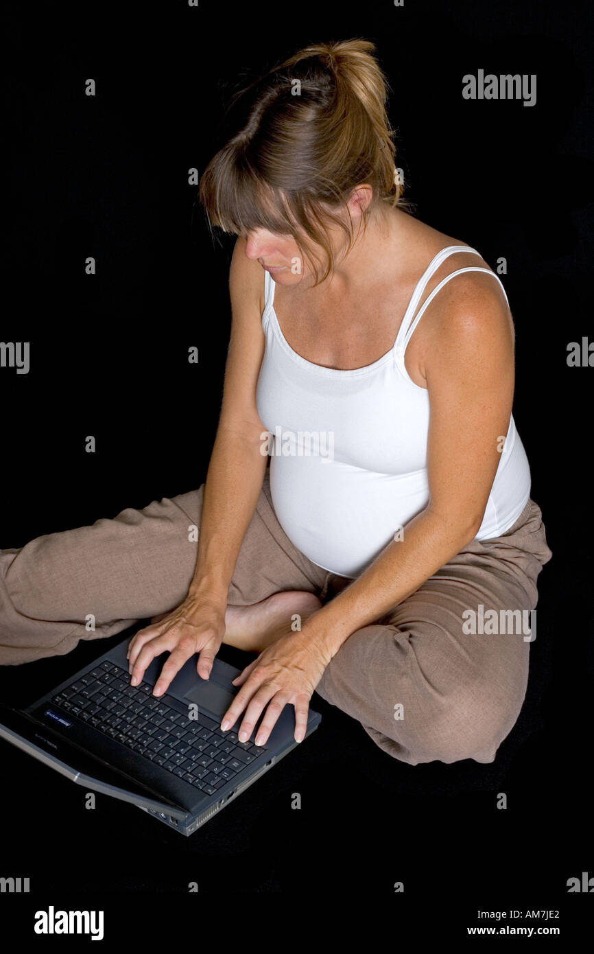 Young expectant pregnant mum sitting and working on a laptop computer ...