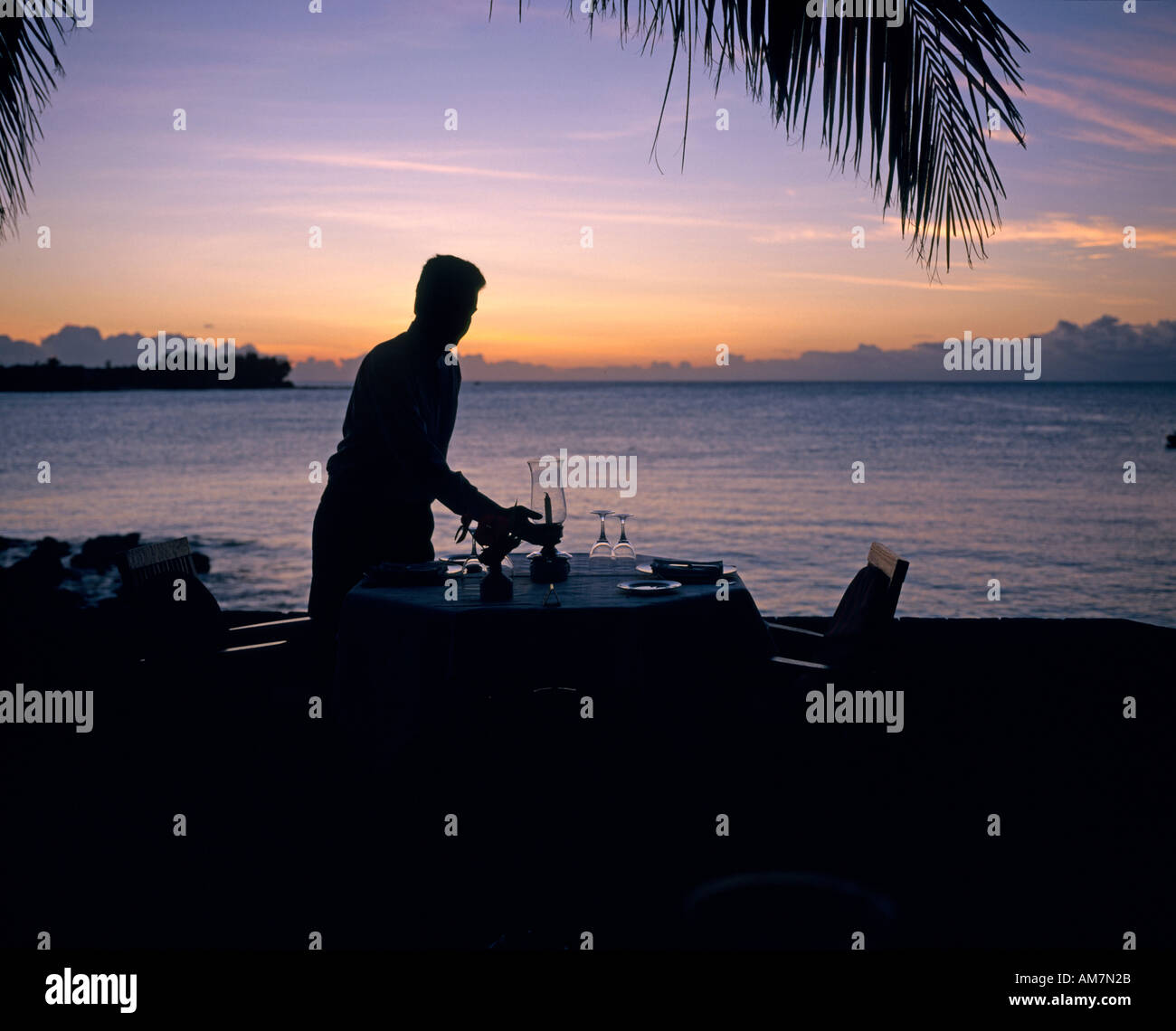 Waiter in silhouette aginst tropical sunset laying table Royal Palm ...