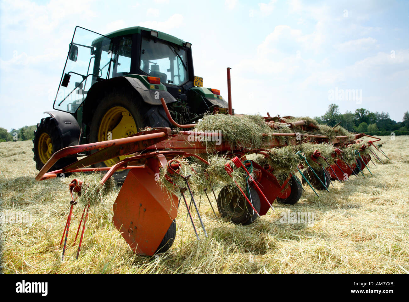 Tractor with tedder fitted to turn summer hay rear view Stock Photo - Alamy