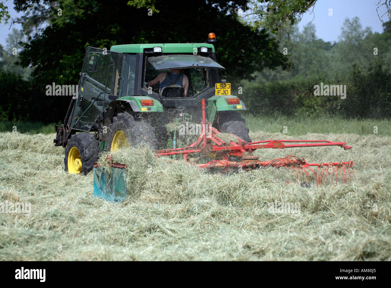 Farmer with tractor and rake rowing hay in summer meadow 10 Stock Photo ...