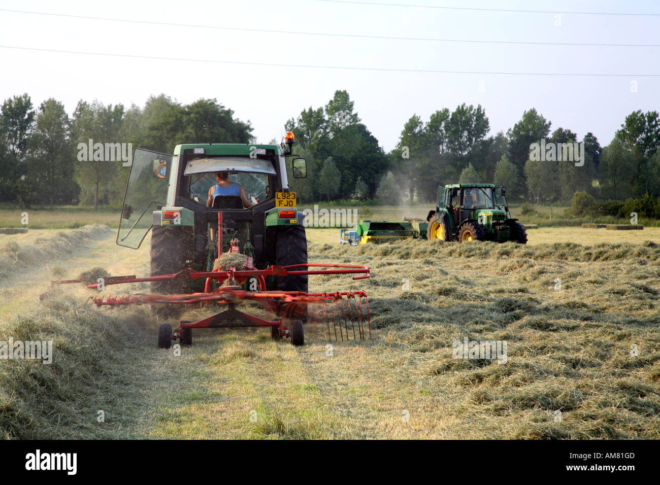 Female farm worker raking hay into rows with tractor with baler at work ...