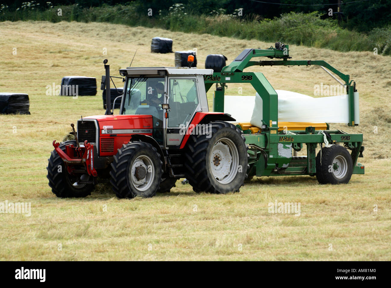 Wrapping big hay bales with tractor and trailer in summer meadow 2 ...