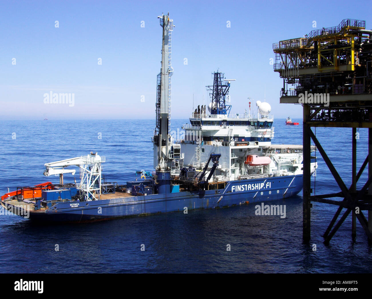 A ship alongside an offshore oil rig with blue skies and calm seas ...