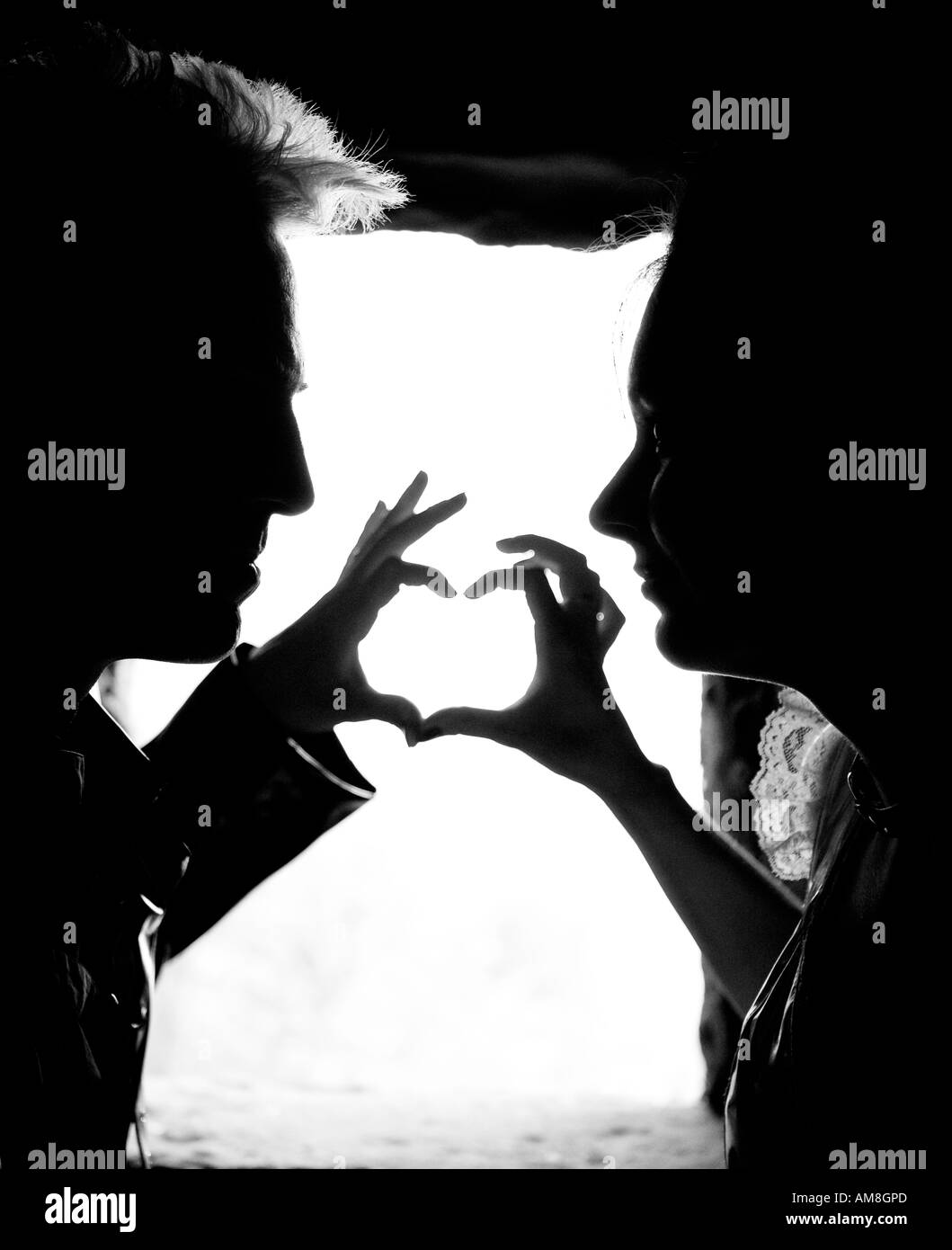 A gothic couple making a heart shape with their hands infront of an old ...