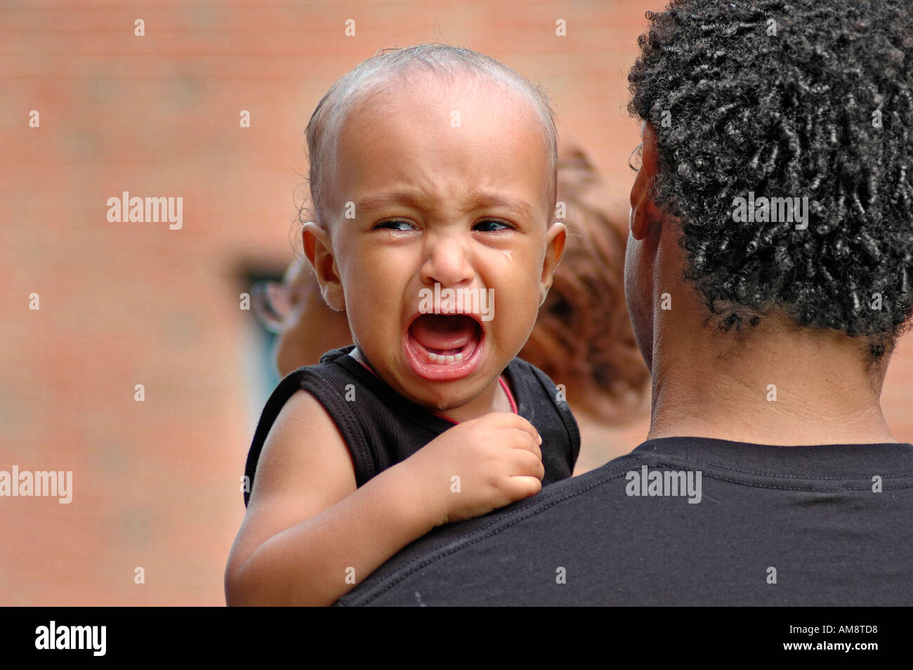 Crying baby being help by dad with mother in background Stock Photo - Alamy