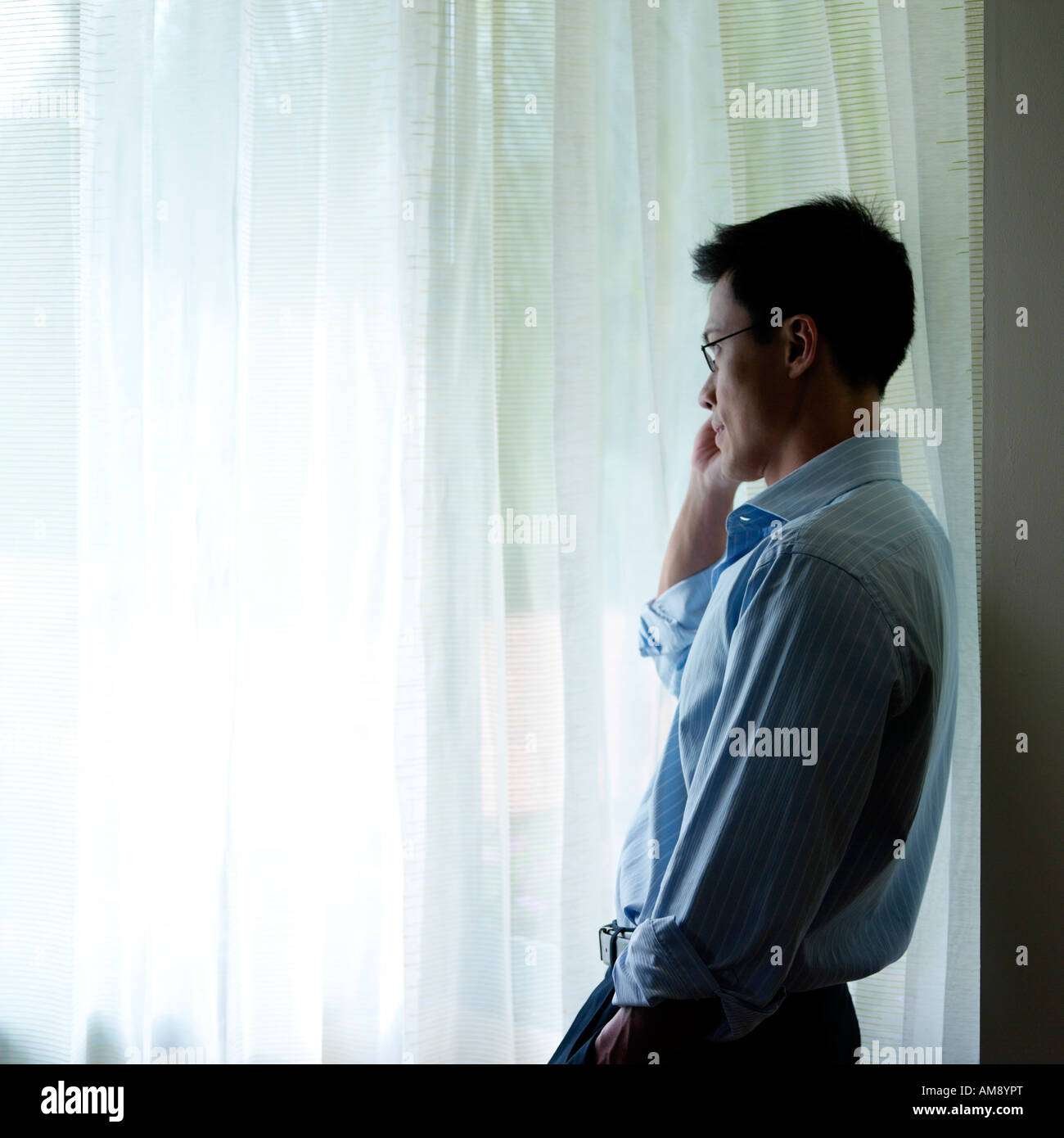 Man standing by window holding mobile phone Stock Photo - Alamy
