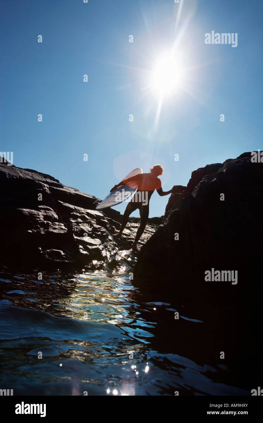 Man walking through large rocks with surfboard Stock Photo - Alamy