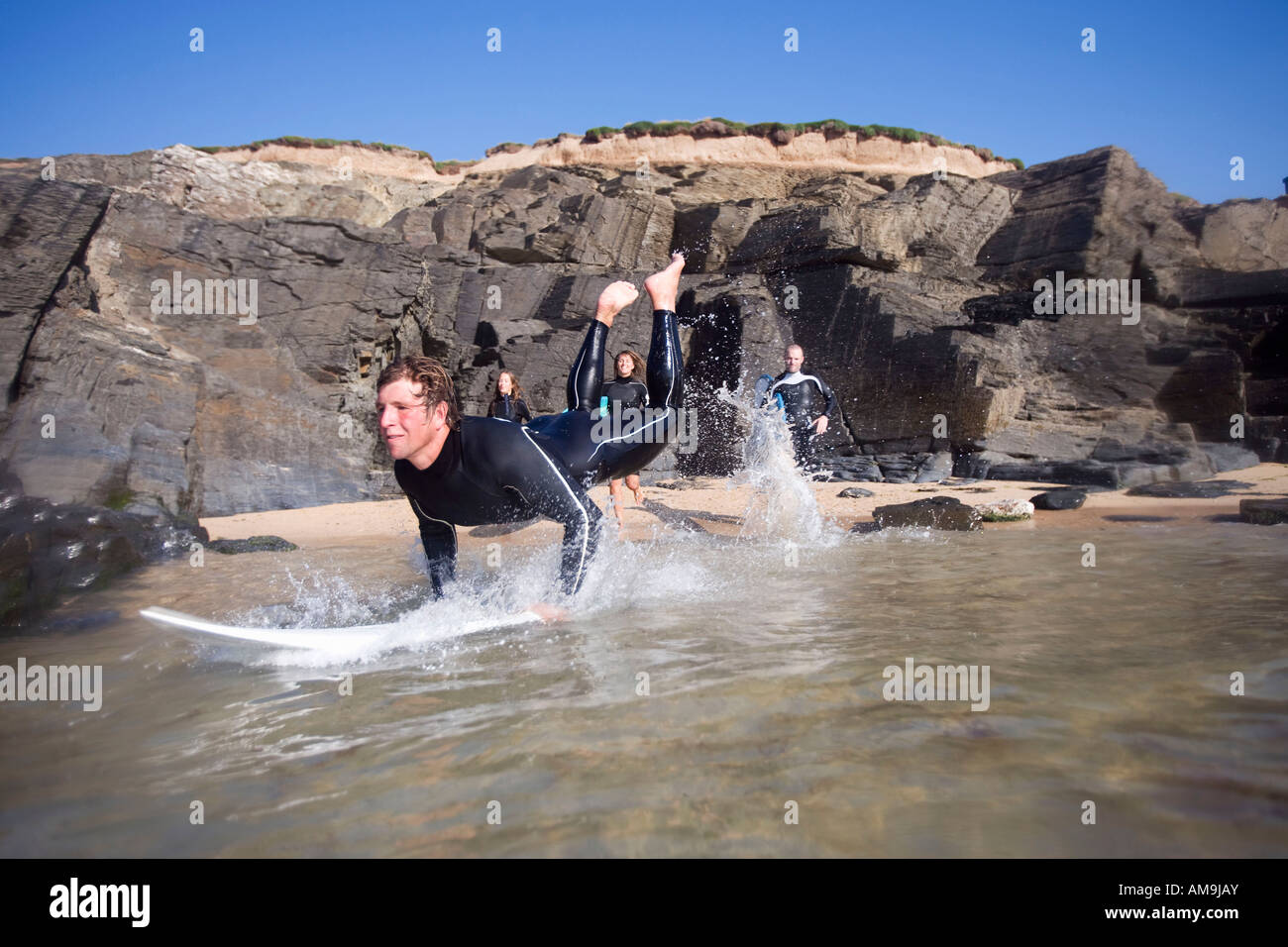 Man on surfboard with three surfers running into water behind him Stock ...