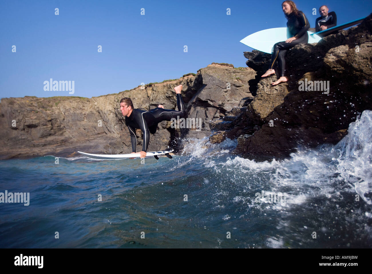 Man jumping into water on surfboard with two people sitting on large ...