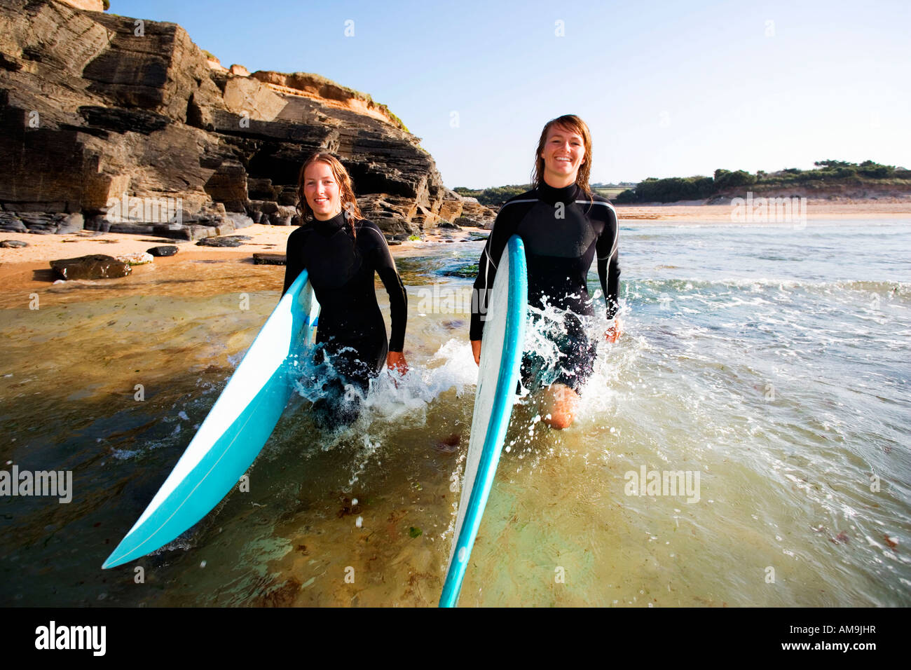 Two women carrying surfboards in the water smiling Stock Photo - Alamy