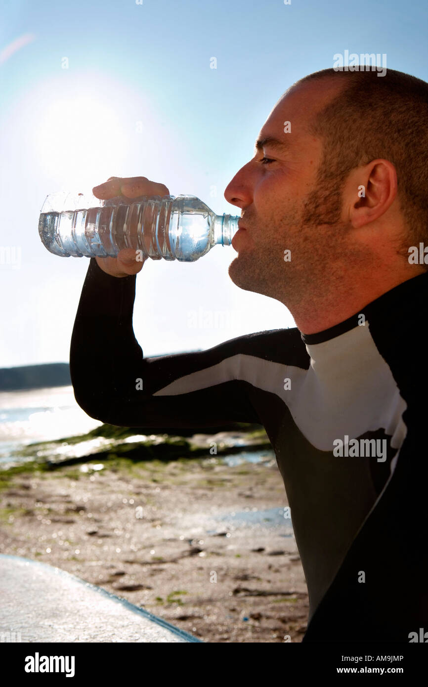 Man sitting with surfboard drinking water Stock Photo - Alamy