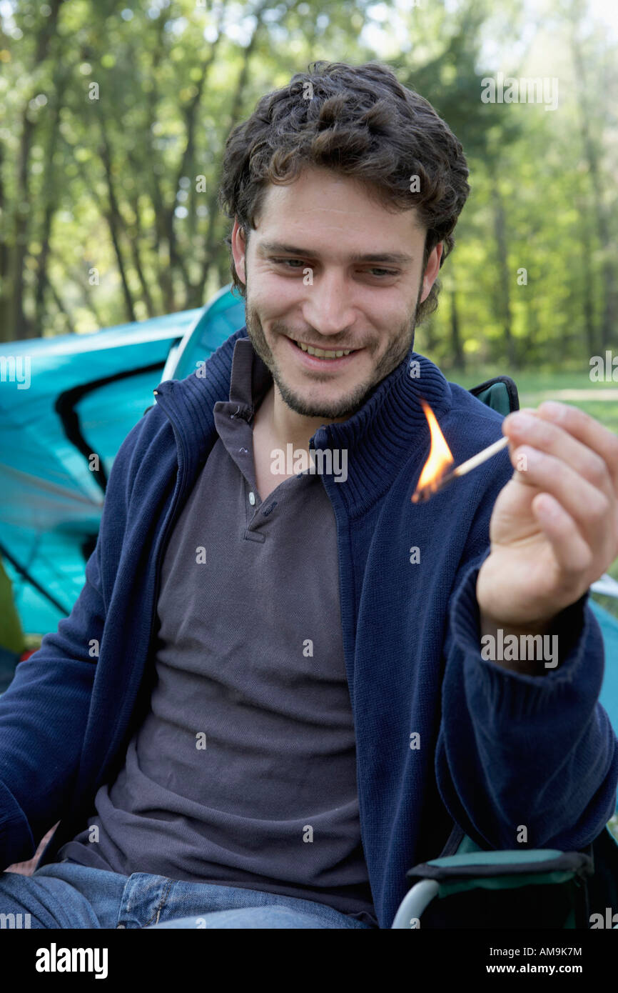 Man sitting at campsite holding a lit match smiling Stock Photo - Alamy