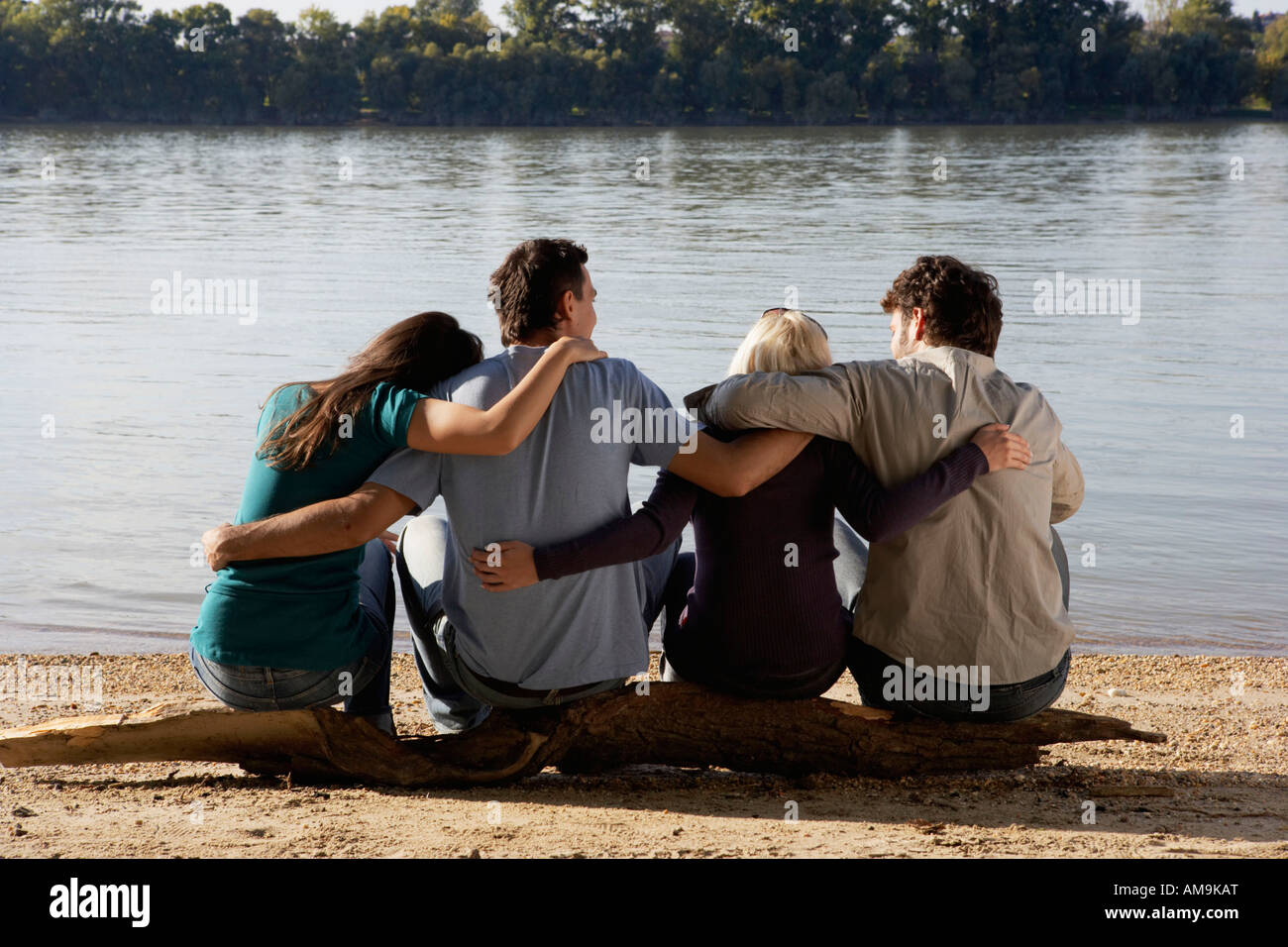 Four friends sitting on log by a lake with arms around each other Stock ...