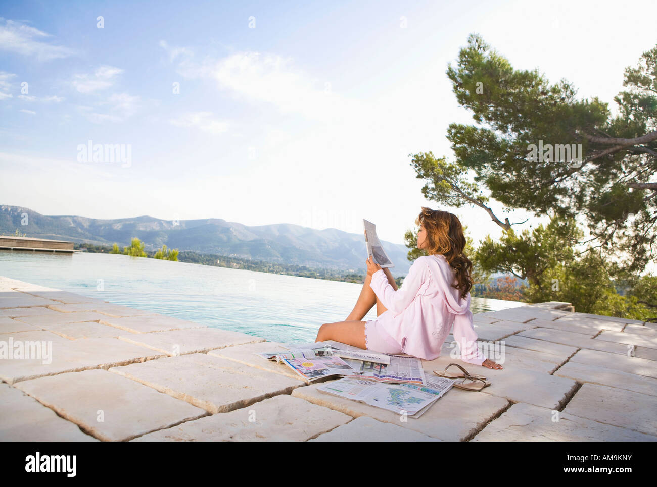 Woman relaxing by infinity pool reading newspaper Stock Photo - Alamy