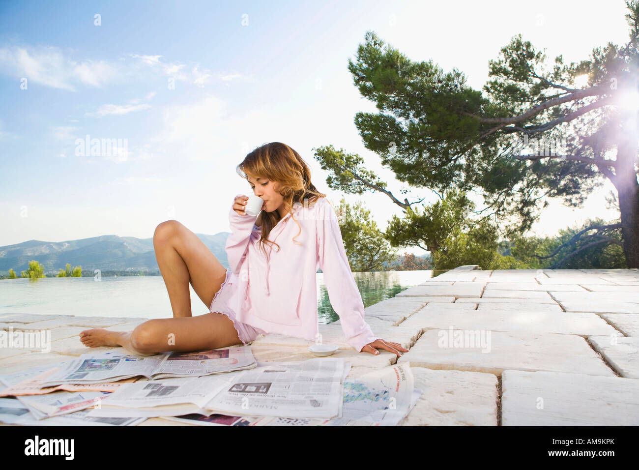 Woman relaxing by infinity pool reading newspaper and drinking coffee ...