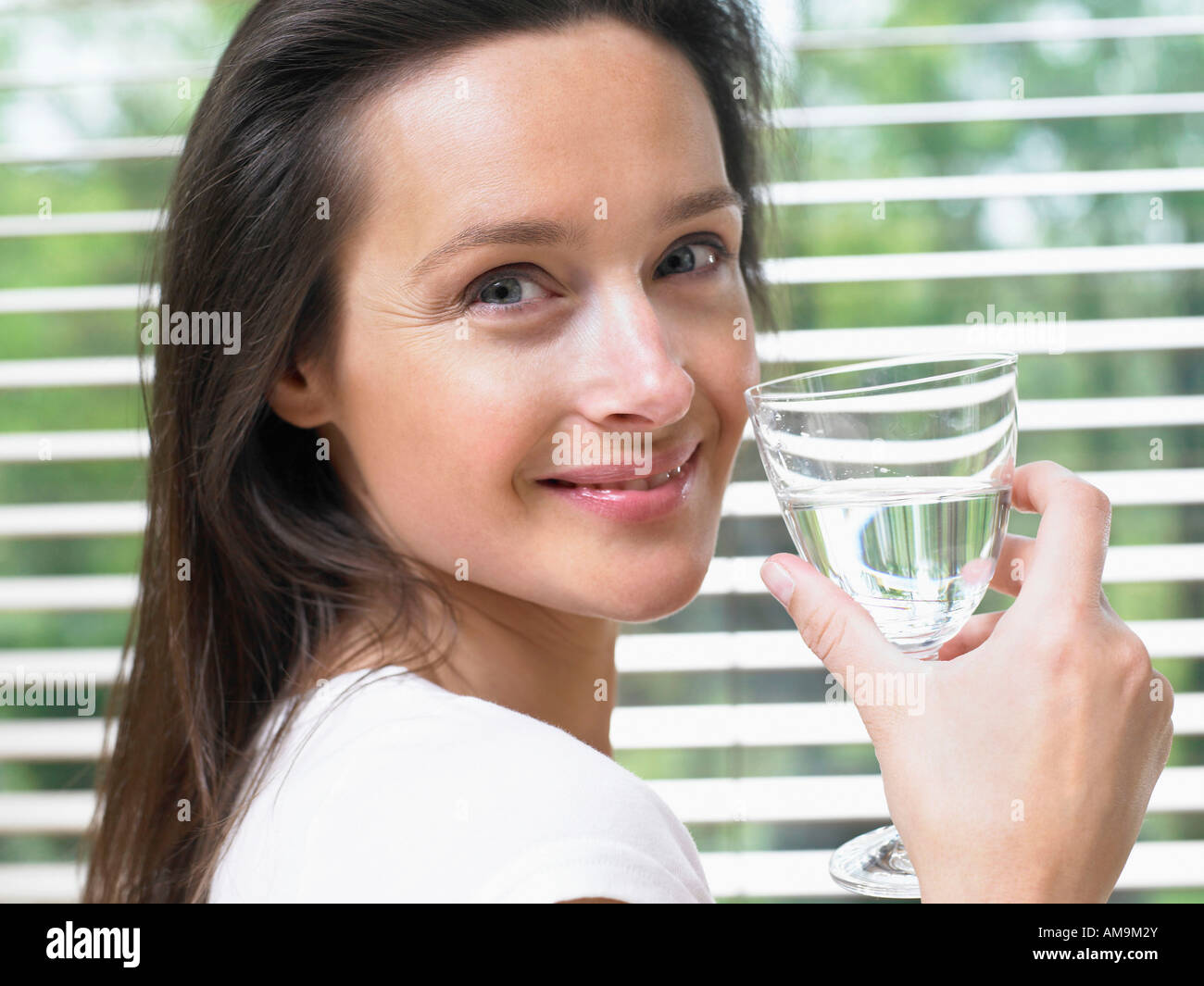 Woman standing by a window holding a glass of water smiling Stock Photo ...