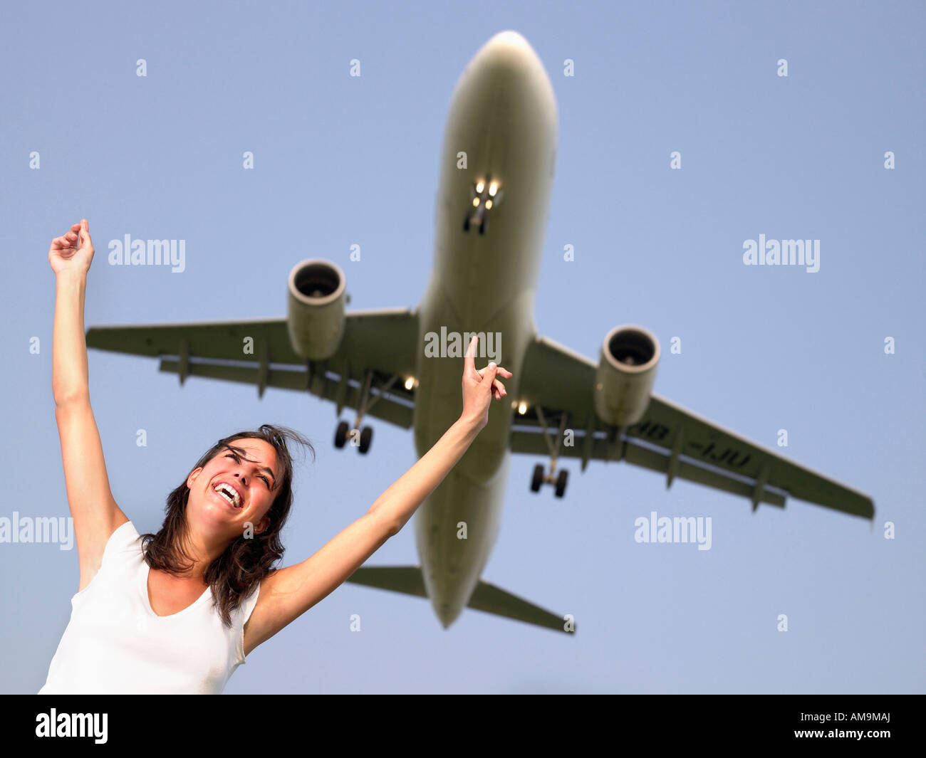 Woman smiling with arms outstretched standing below a plane flying ...