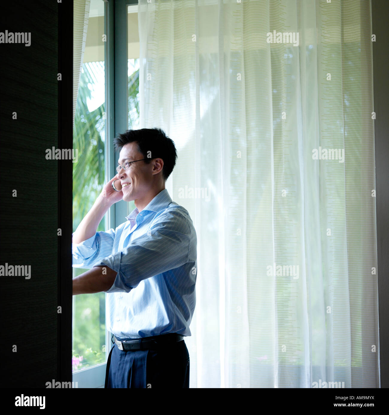 Man standing by window holding mobile phone Stock Photo - Alamy