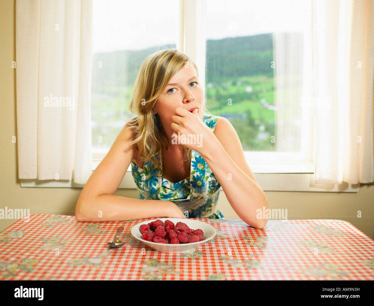 Woman eating bowl of raspberries at table Stock Photo - Alamy