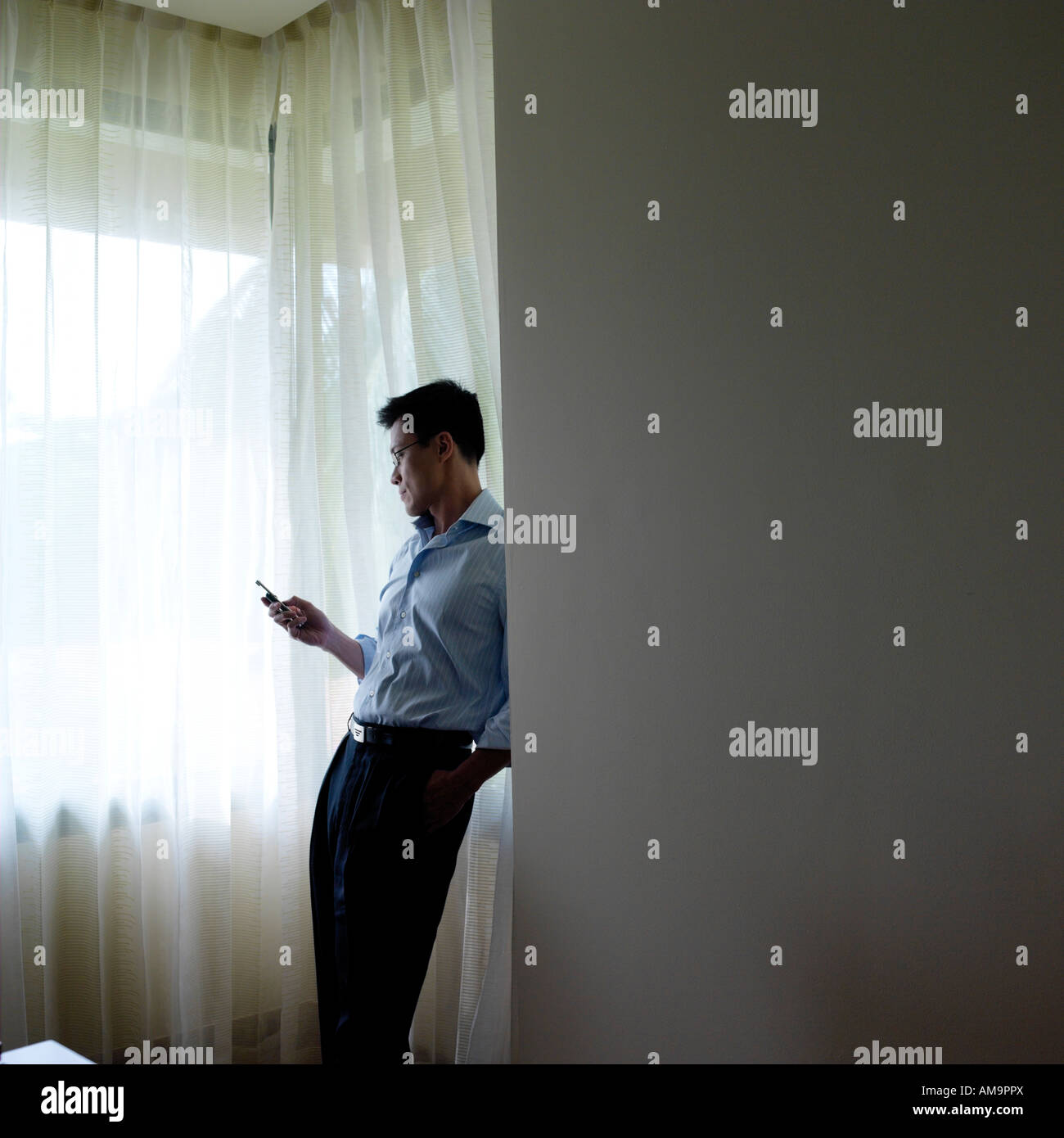 Man standing by window holding mobile phone Stock Photo - Alamy