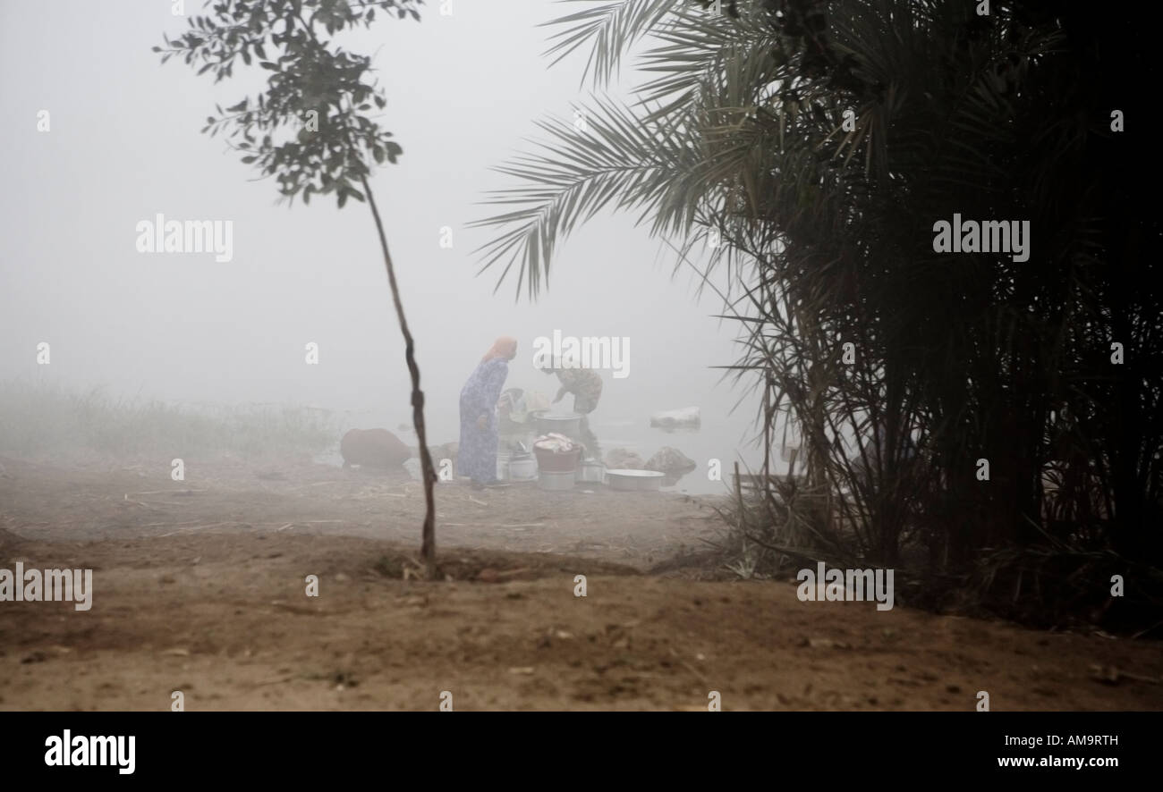 Women washing clothes in river emerging through early morning mist ...