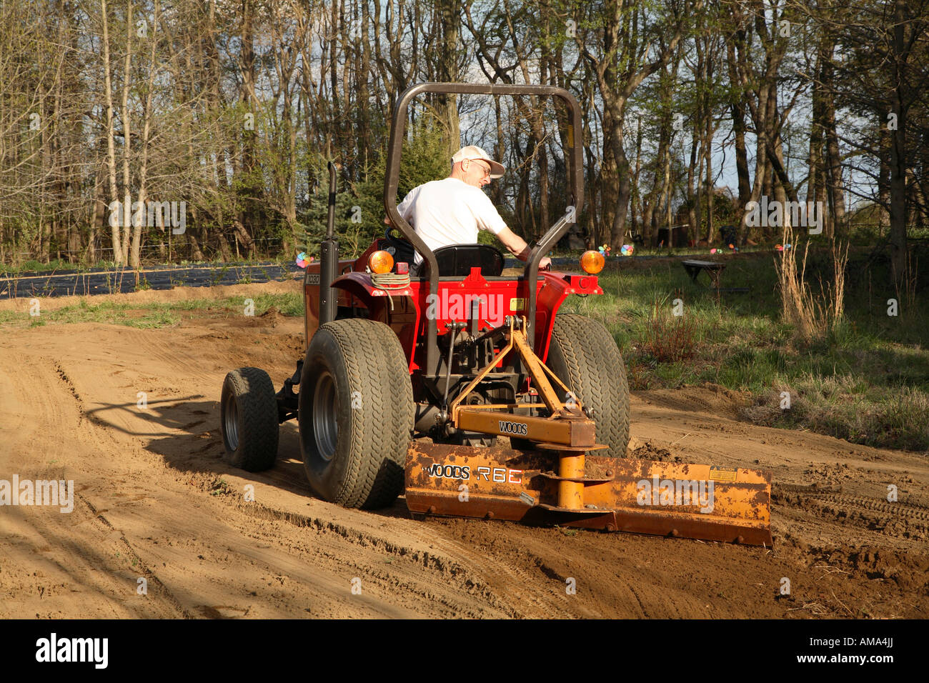 Man driving small tractor and scraping field with flat grading blade ...
