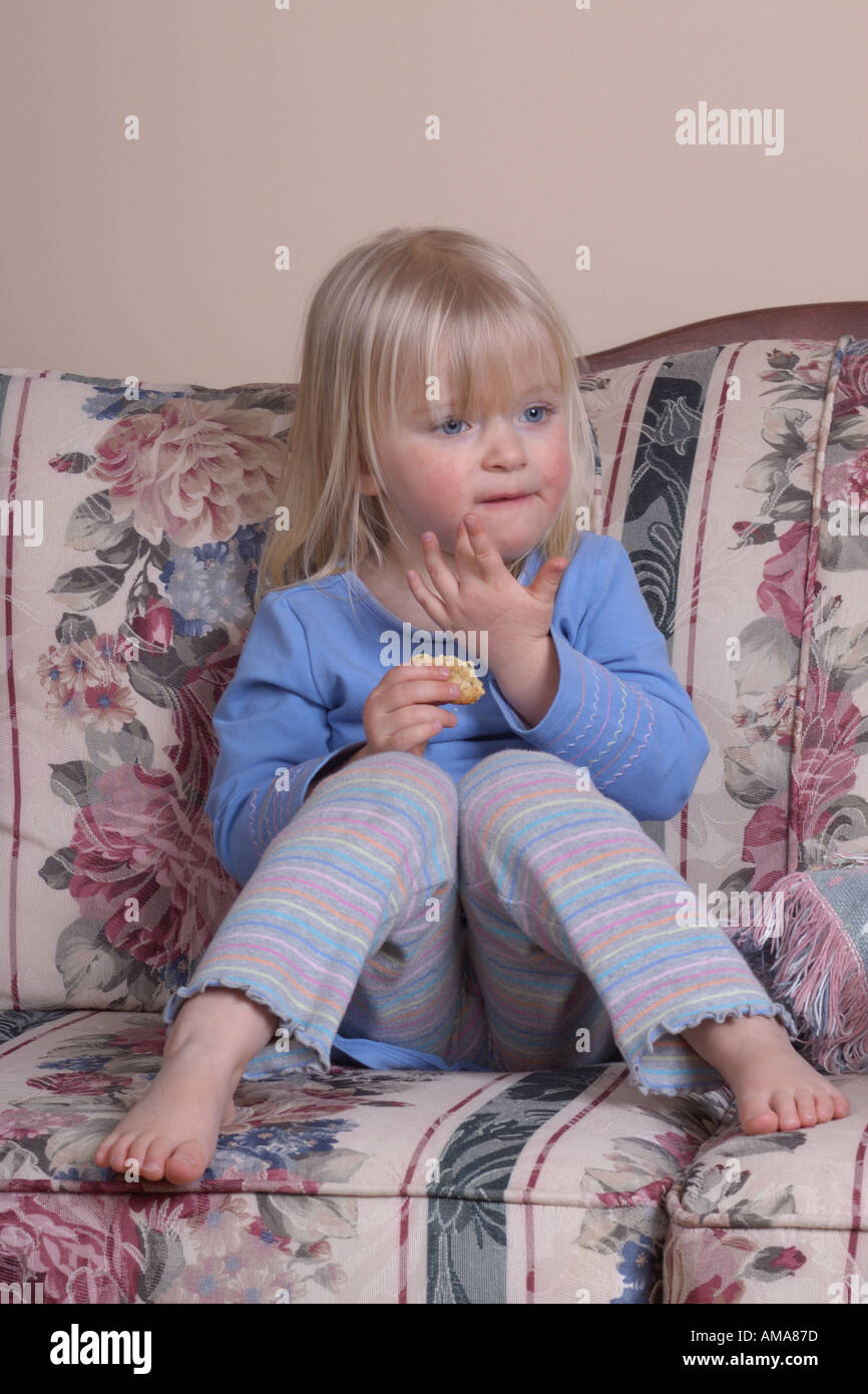 young girl sitting on couch holding a cracker Stock Photo - Alamy
